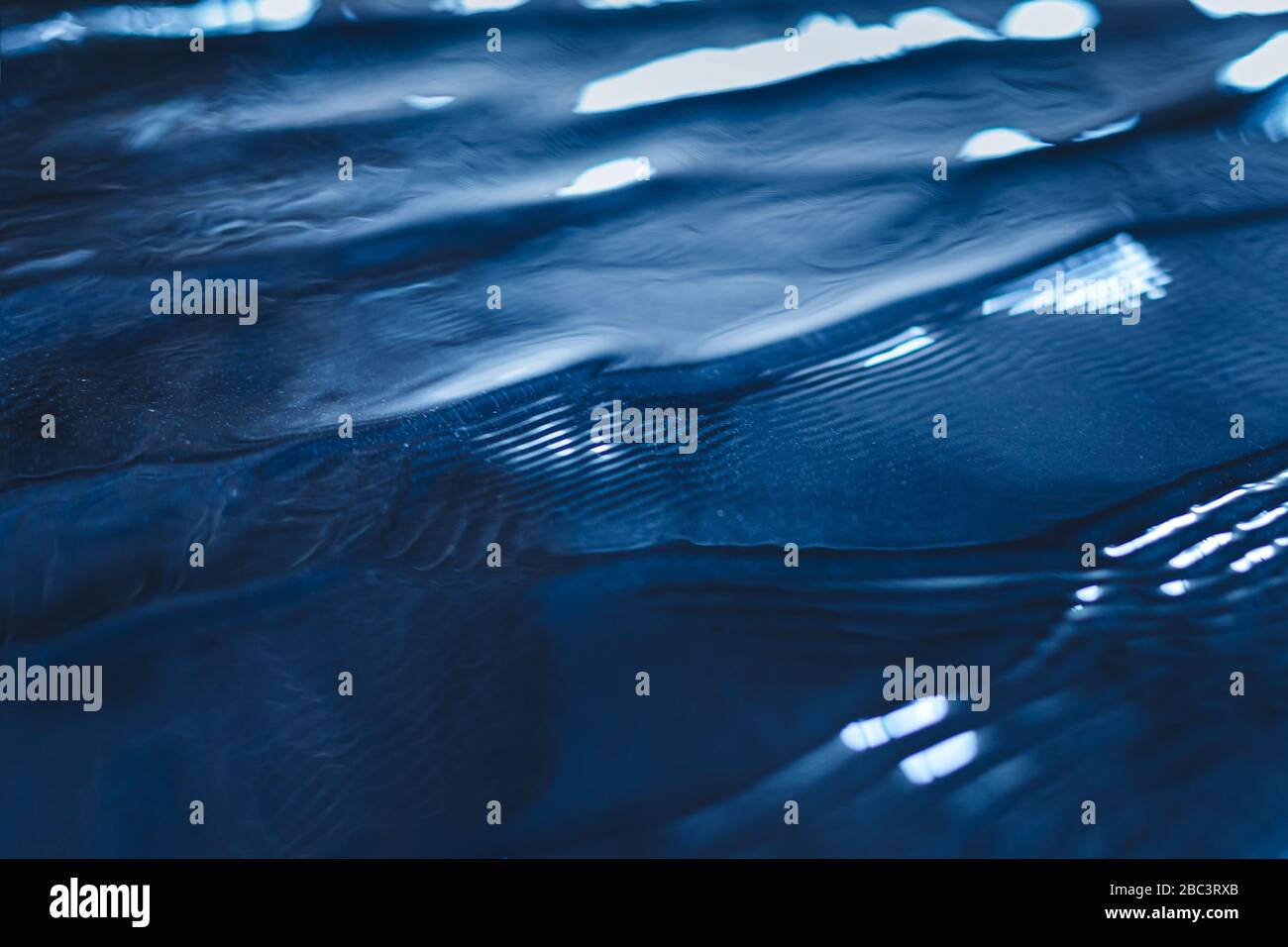 Closeup of calm water surface texture with waves in dark blue color ...