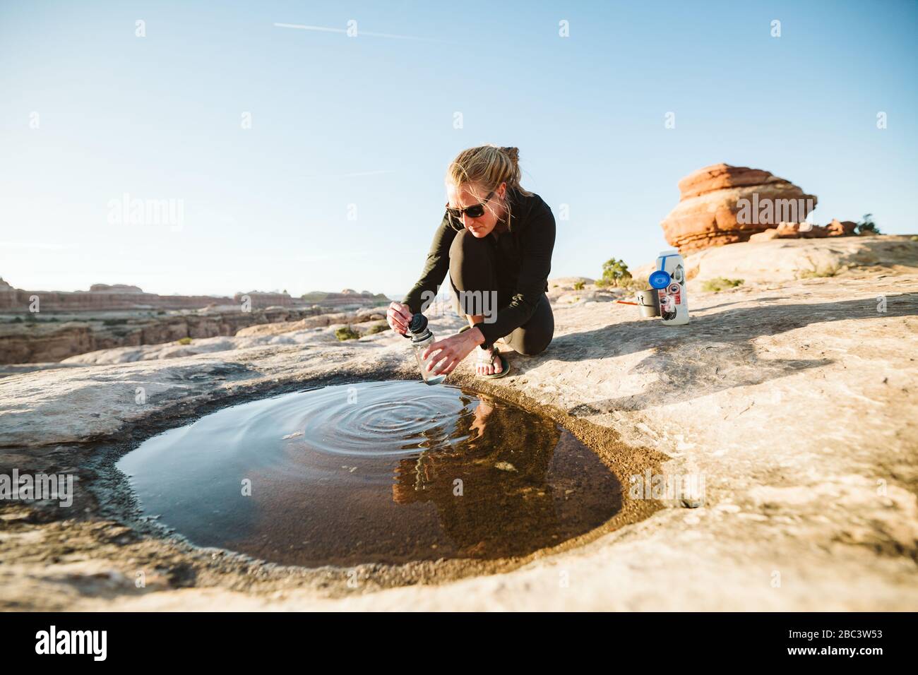 hiker collects drinking water from a shallow puddle in the desert Stock ...