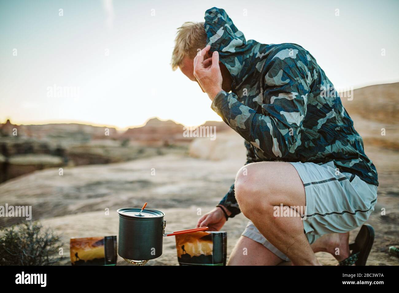 male camper prepares camp dinner and pulls camo jacket over head Stock ...