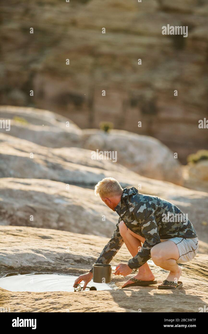 blonde man scoops water from a shallow puddle in the desert Stock Photo ...