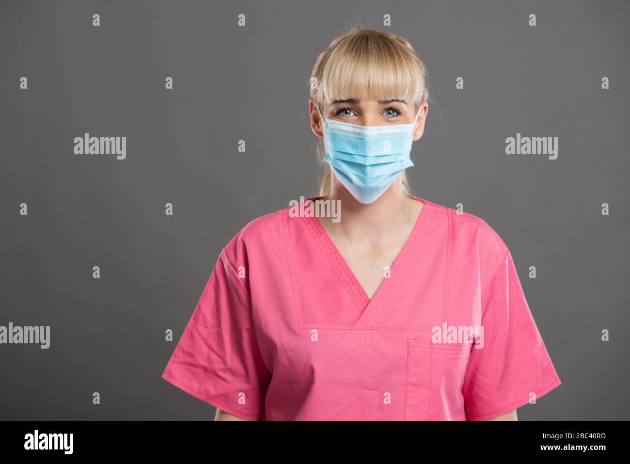 Portrait of young attractive female nurse wearing face mask on gray ...