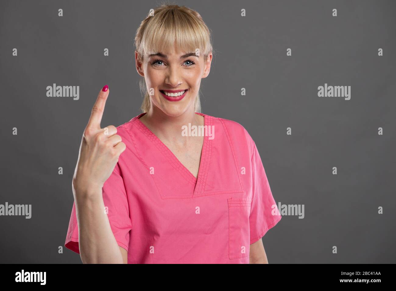 Portrait of young attractive female nurse showing number one on gray ...
