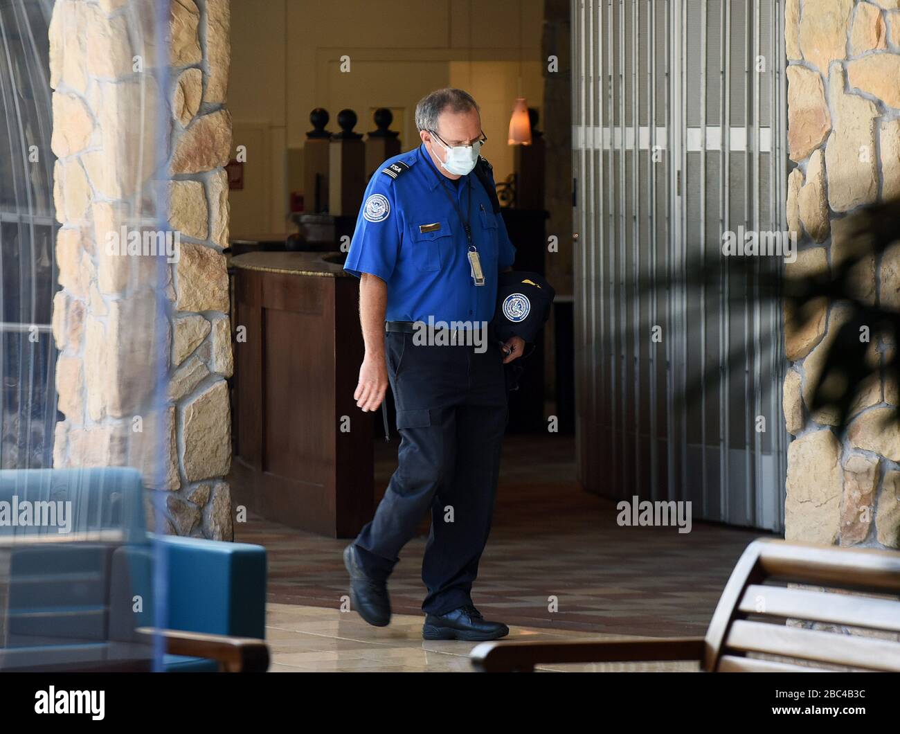 A TSA officer wears a protective mask as a preventive measure against ...