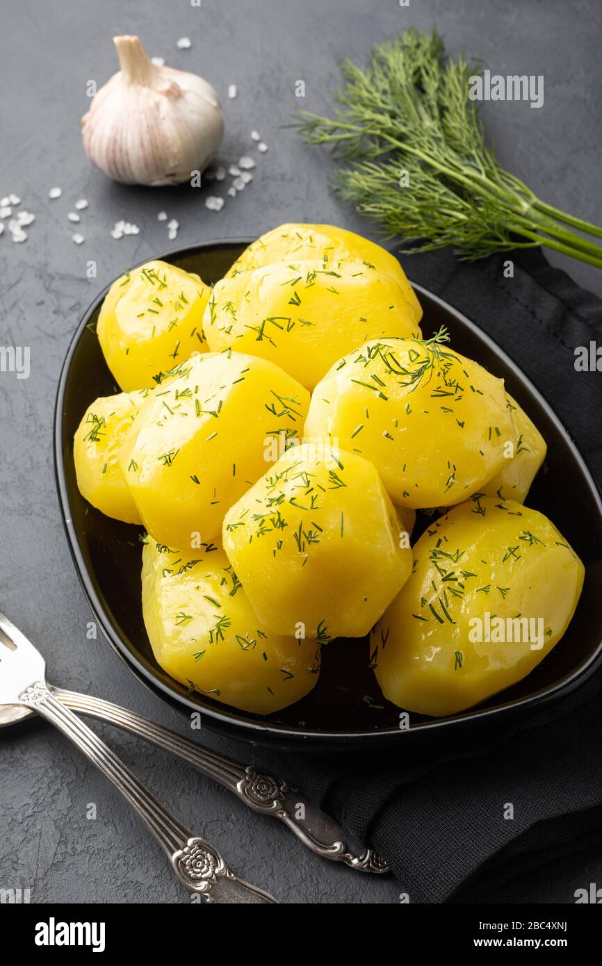 Boiled potatoes with herbs in rustic bowl with silverware, salt, garlic ...