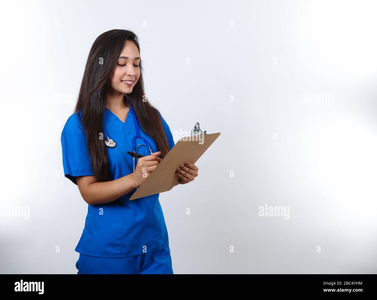 A pretty nurse in blue scrubs writes notes on her clip board Stock ...