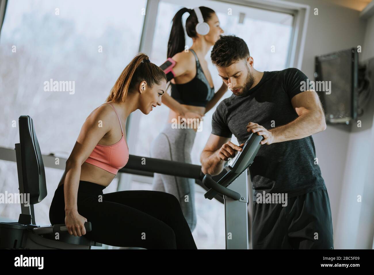 Personal trainer with pretty young woman on cycling machine at the gym ...