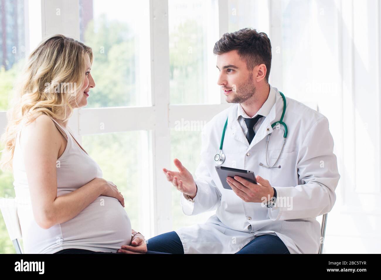 Pregnant woman visiting young doctor Stock Photo - Alamy