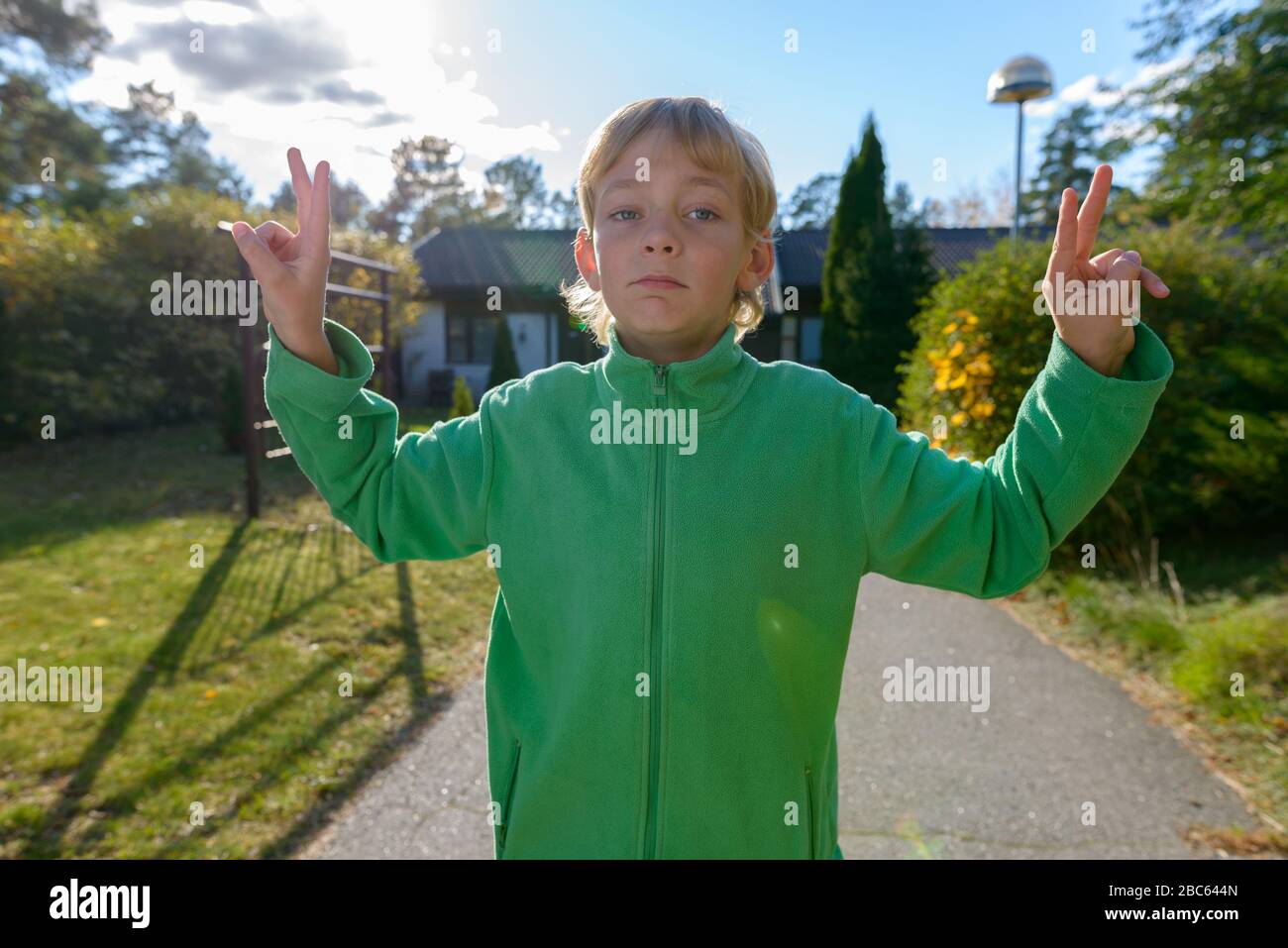 Young handsome boy giving peace sign with both hands in the front yard ...