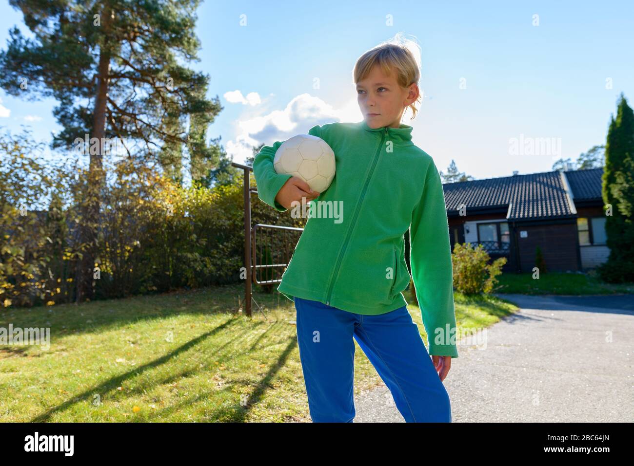 Young handsome boy thinking while holding soccer ball in the front yard ...