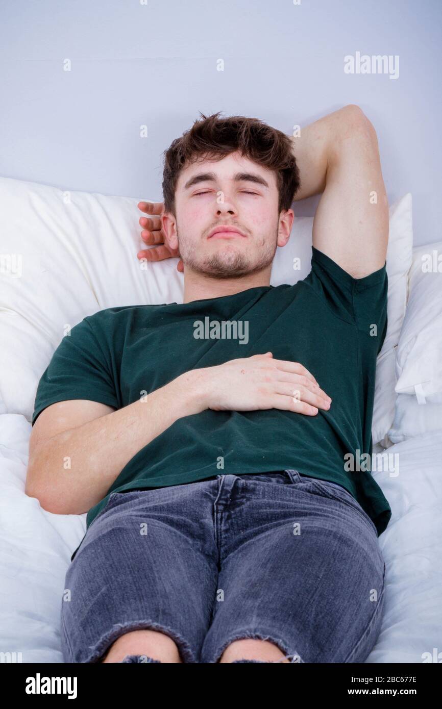 A young adult man laying on his back sleeping in his clothes on a bed ...