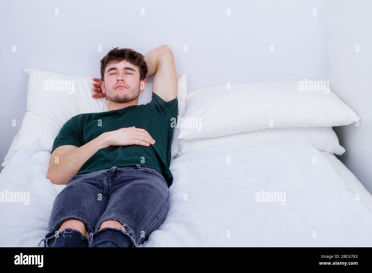 A young adult man laying on his back sleeping in his clothes on a bed ...