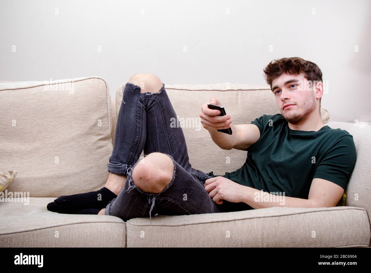 A young adult man using a remote control while on a sofa Stock Photo ...