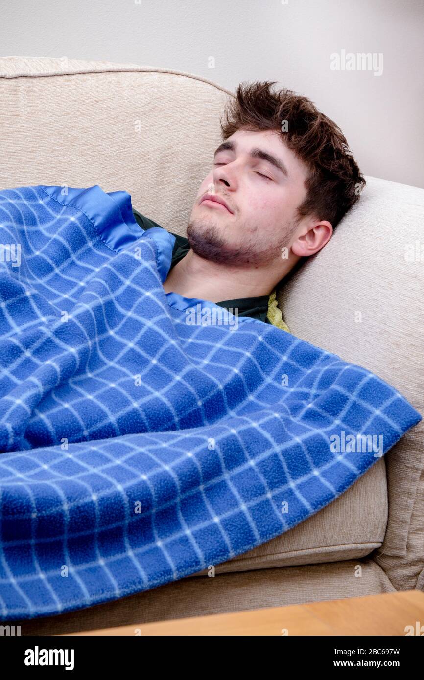 A young adult man asleep on a sofa, with a blanket Stock Photo - Alamy