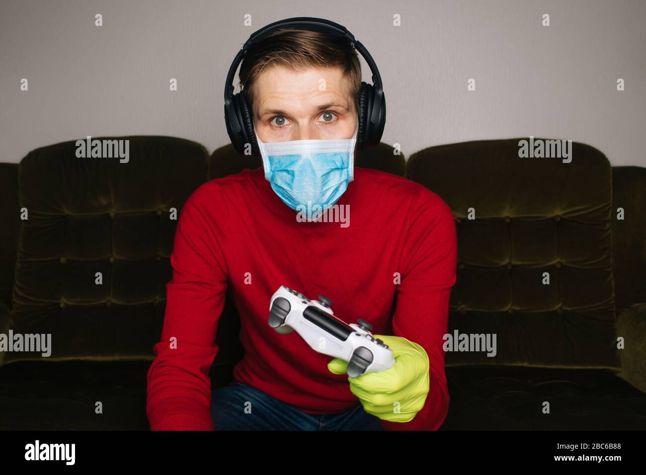 Man playing video game wearing a surgical mask, rubber gloves and noise ...