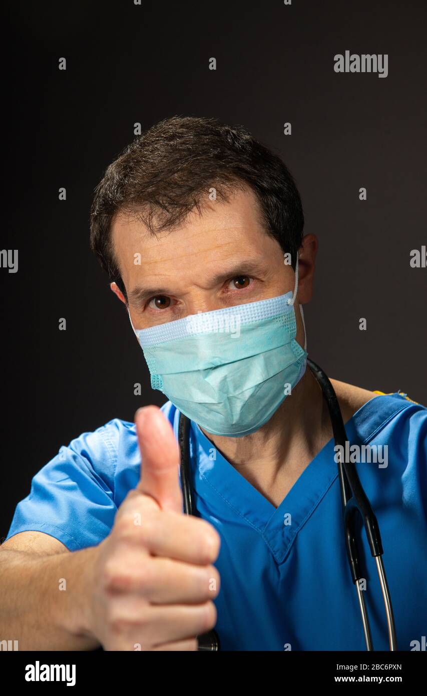 Concerned doctor doing a thumbs up hand gesture and wearing blue ...