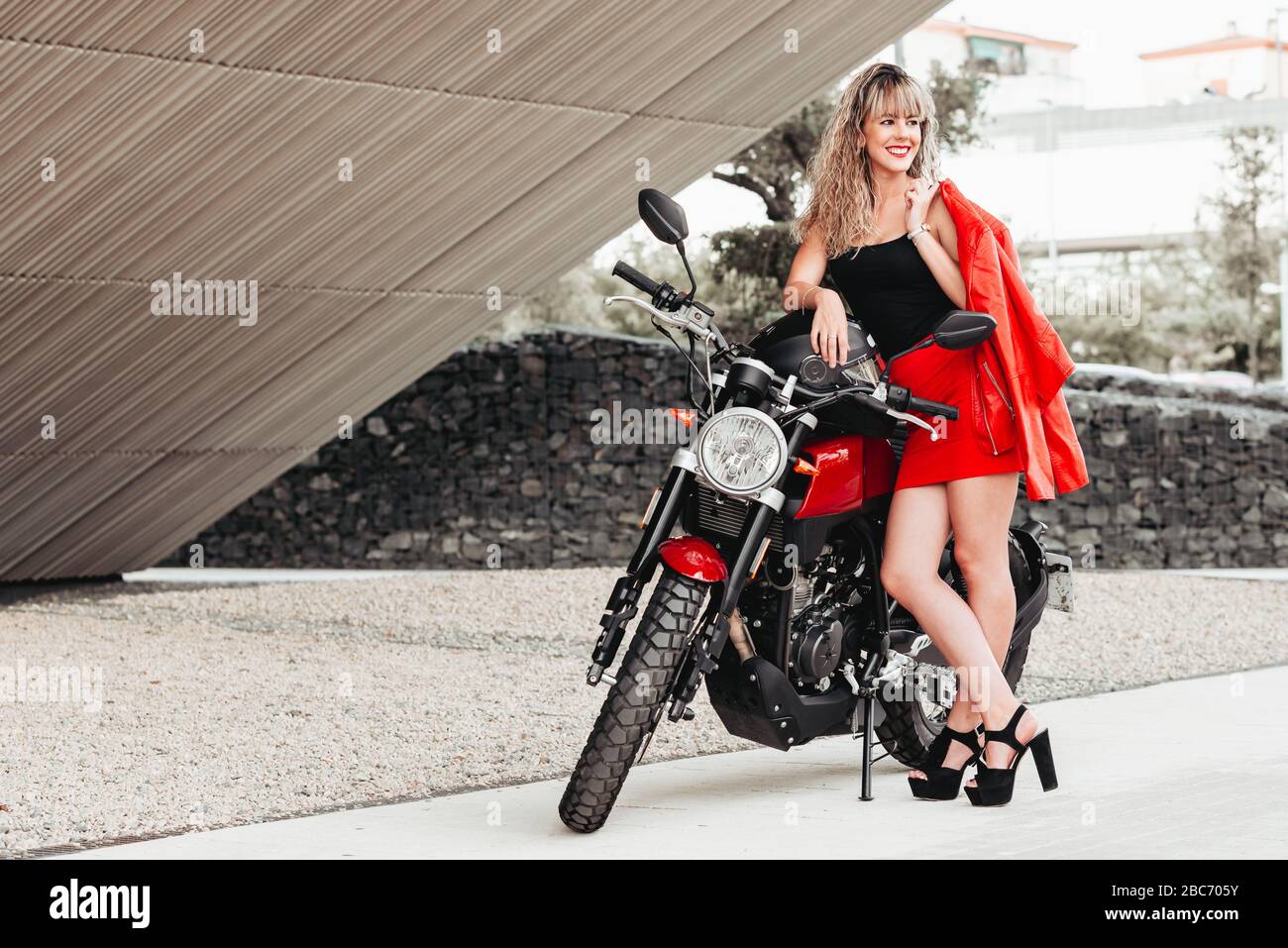 blonde woman with red jacket and mini-skirt on a vintage motorcycle ...