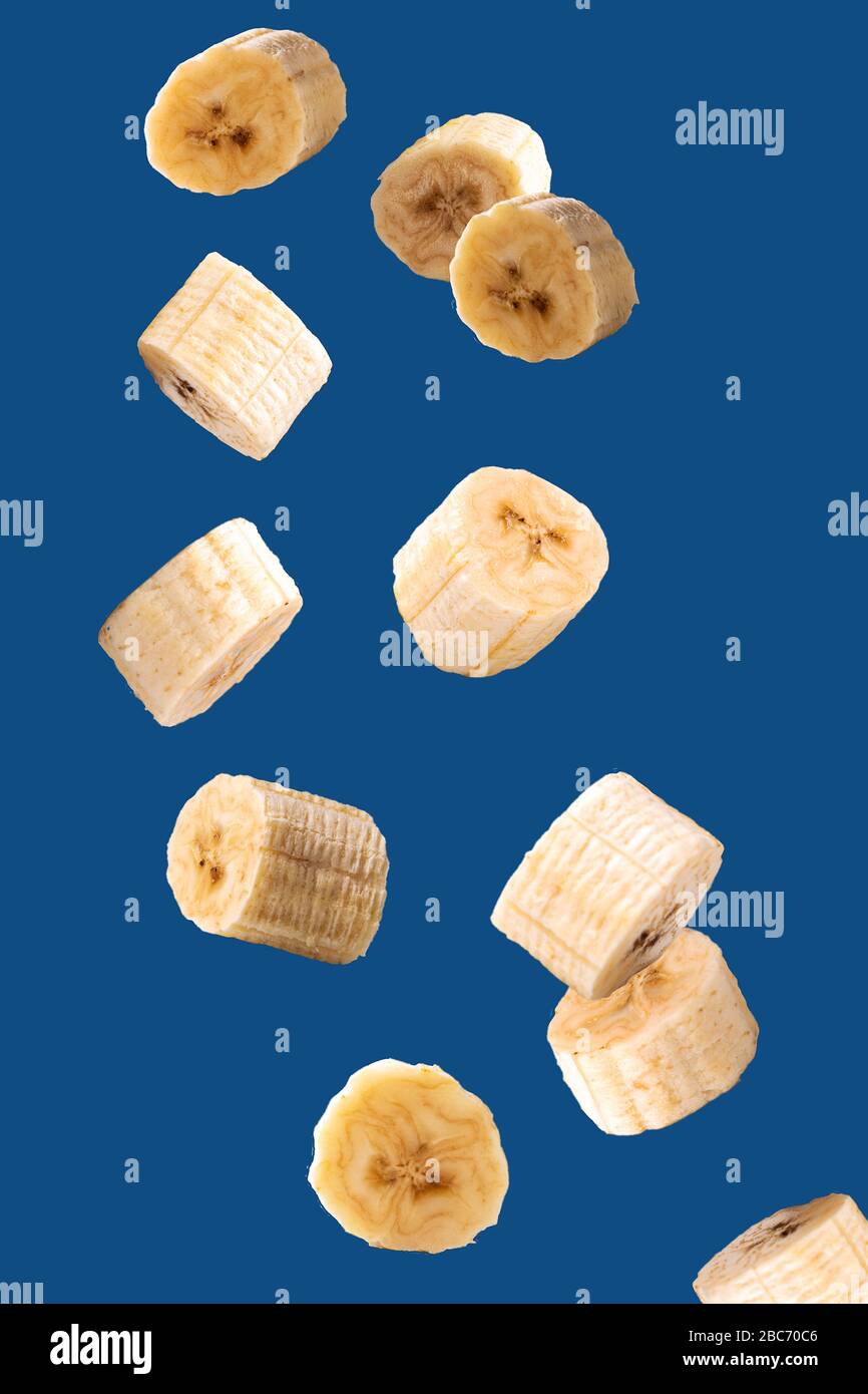 Flying food. Falling sliced banana fruit over trendy classic blue ...