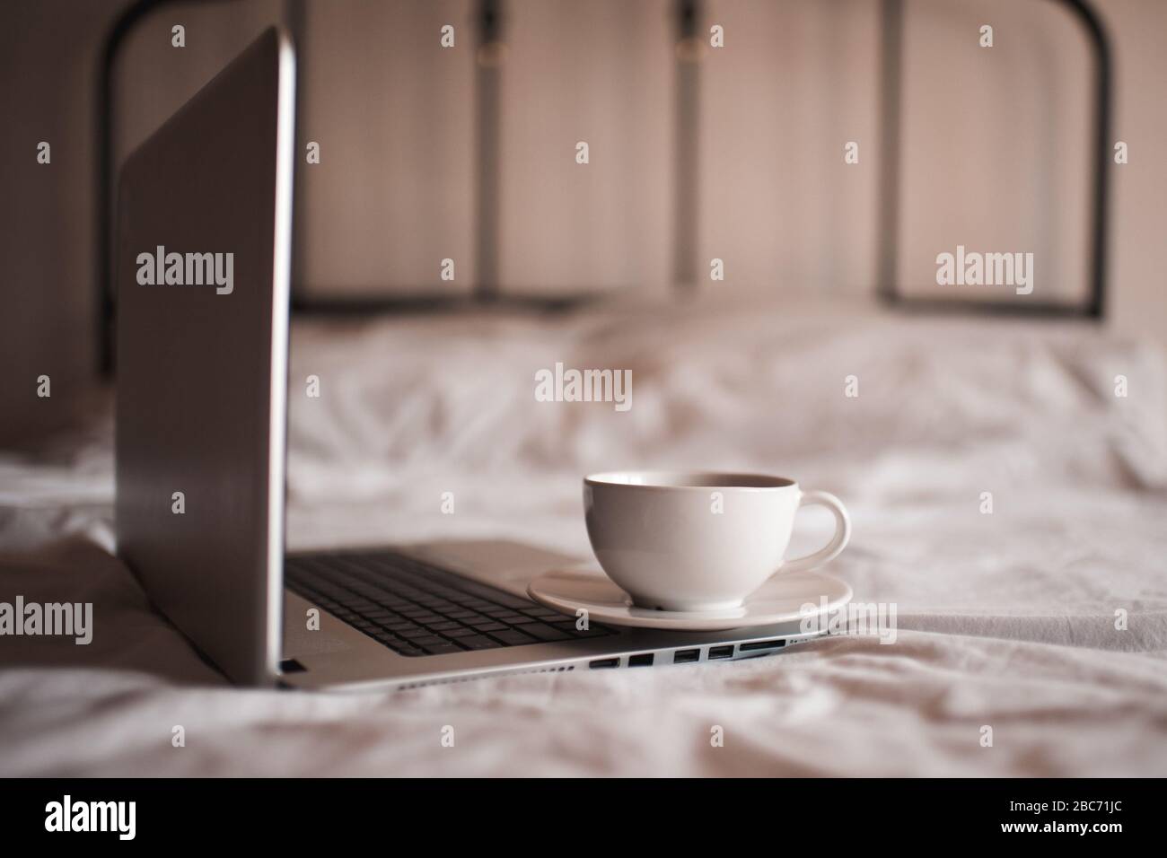 Working at home concept. Cup of coffee staying on open computer in bed ...