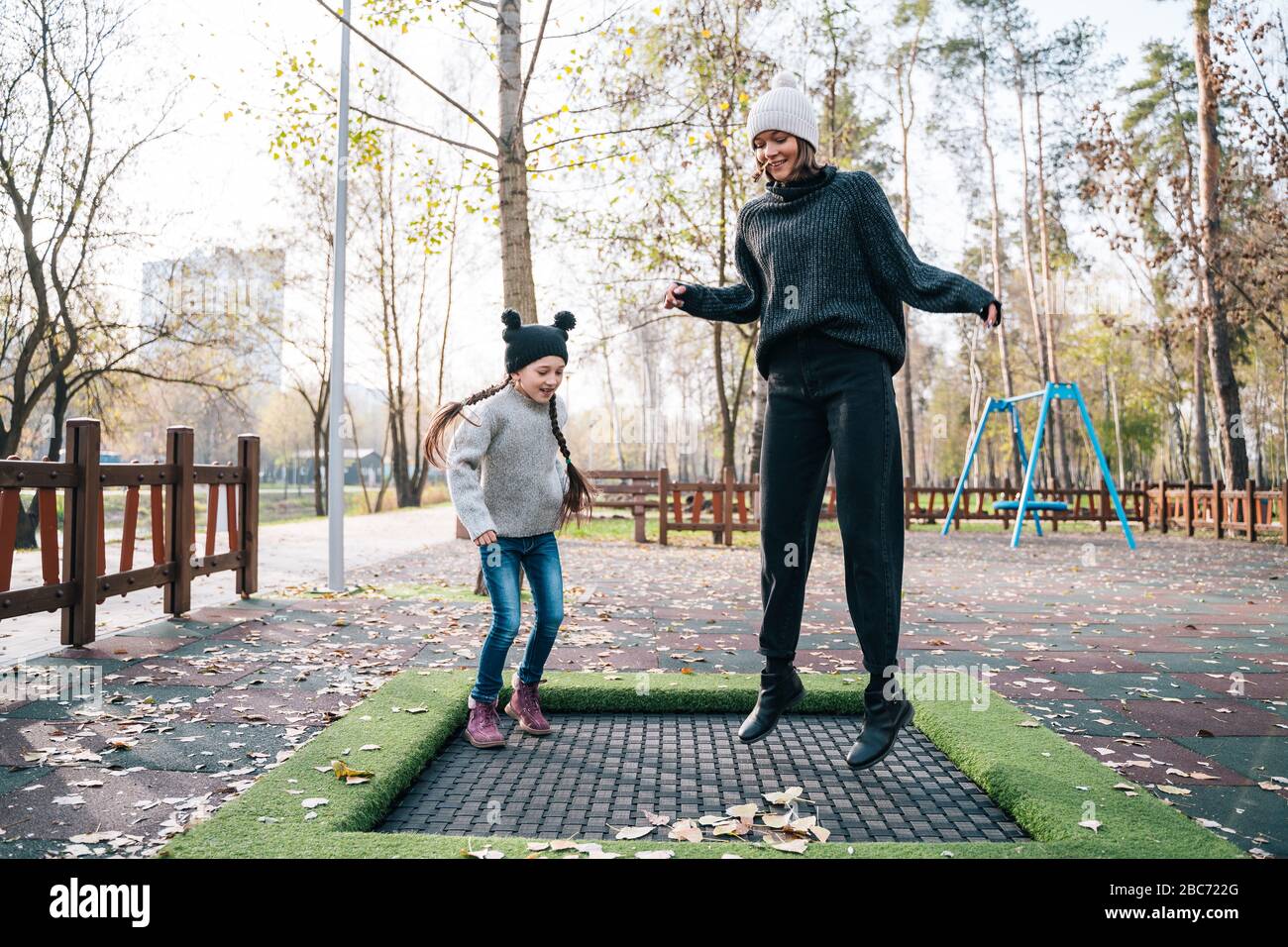 Mom And Her Daughter Jumping Together On Trampoline In Autumn Park