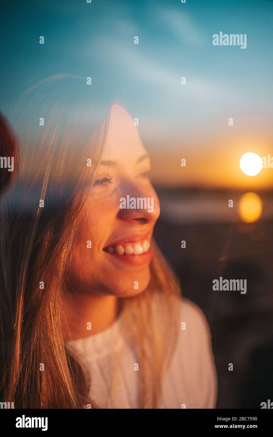 Young woman behind a window. You can see the reflection of a sunset ...