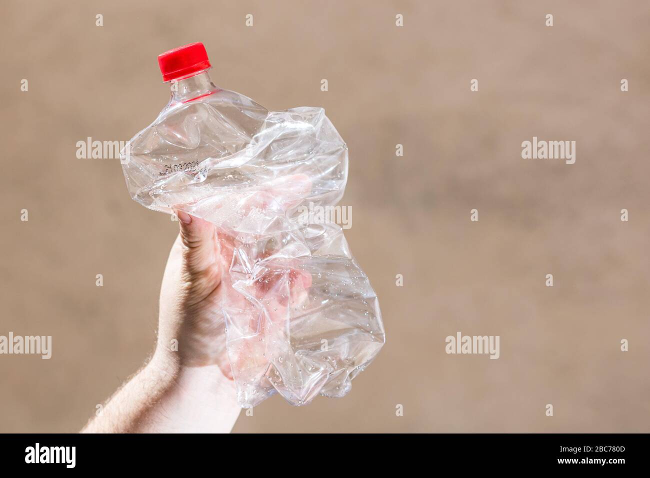 Hand holding smashed empty plastic bottle isolated on a blurred ...
