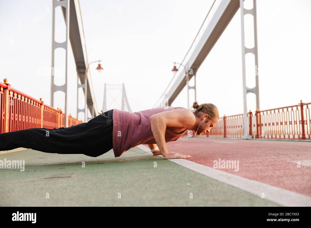 Attractive young fit sportsman working out on a bridge, doing push-ups ...