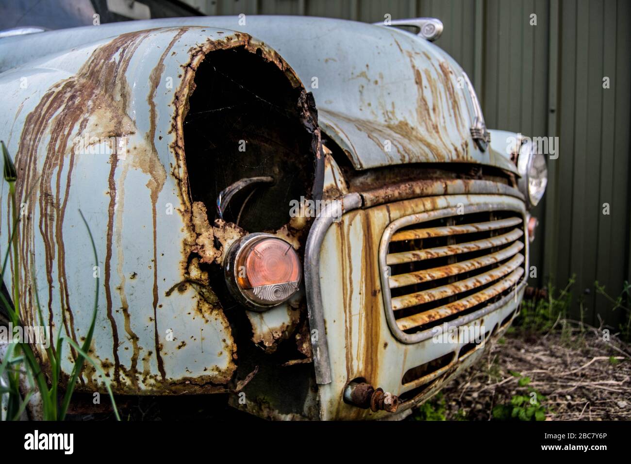 A closeup of the front of a rusted old car with a missing headlight ...