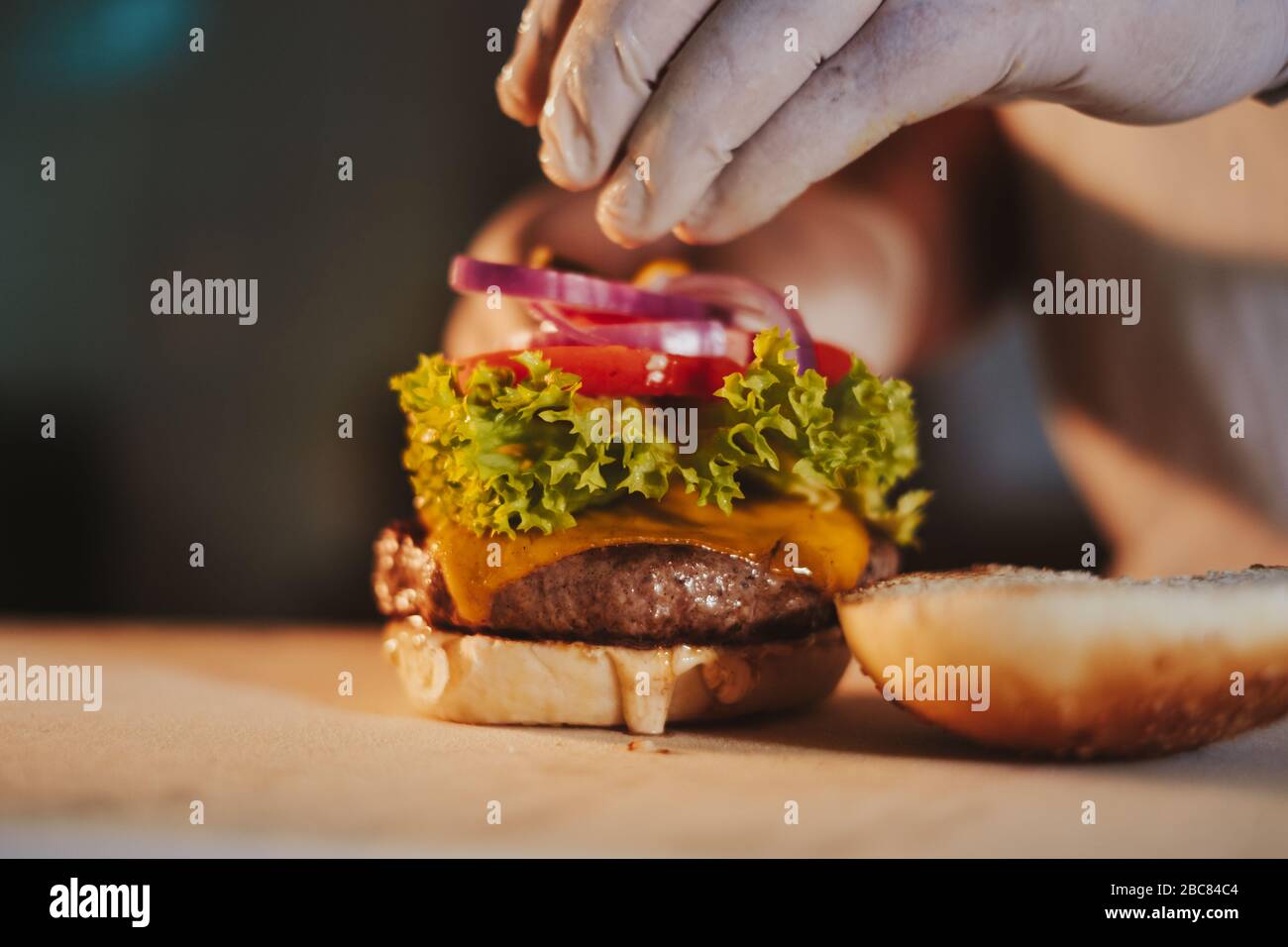 Kitchen chef assembling cheeseburger by adding onion with gloves on ...