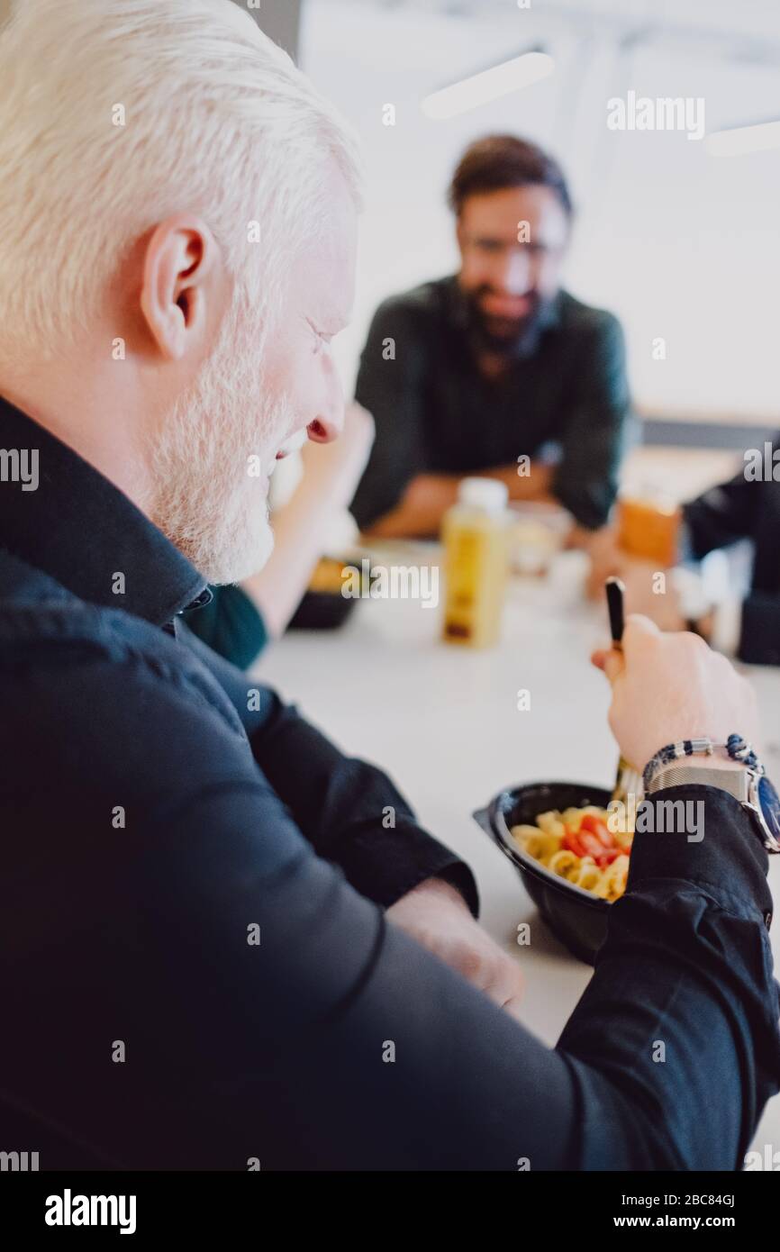Man eating pasta in the office cafeteria and smiling with his ...