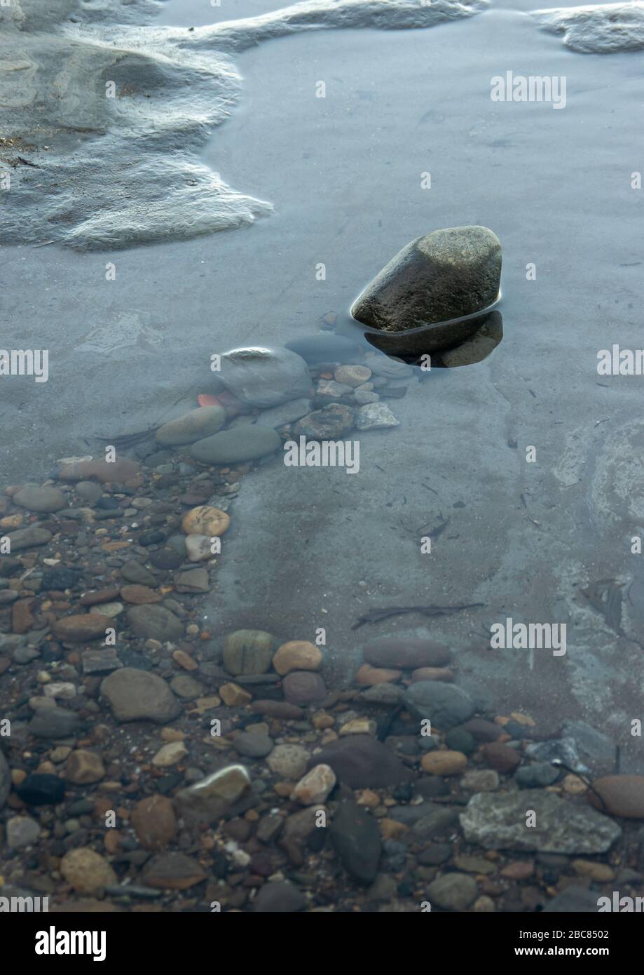 A single rock above the surface in a rock pool with submerged pebbles ...