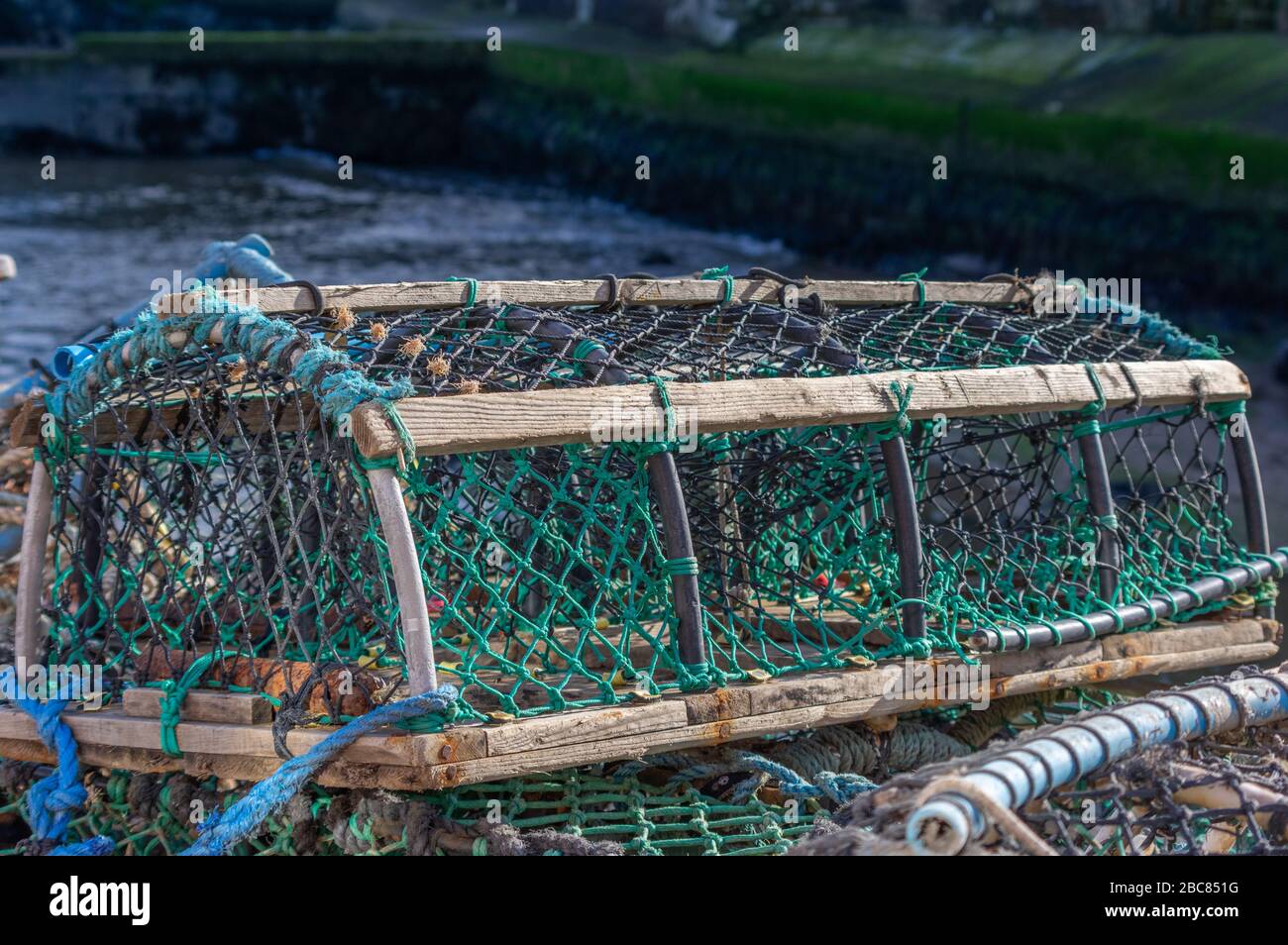 A single traditional lobster pot with a harbour wall and water in the ...