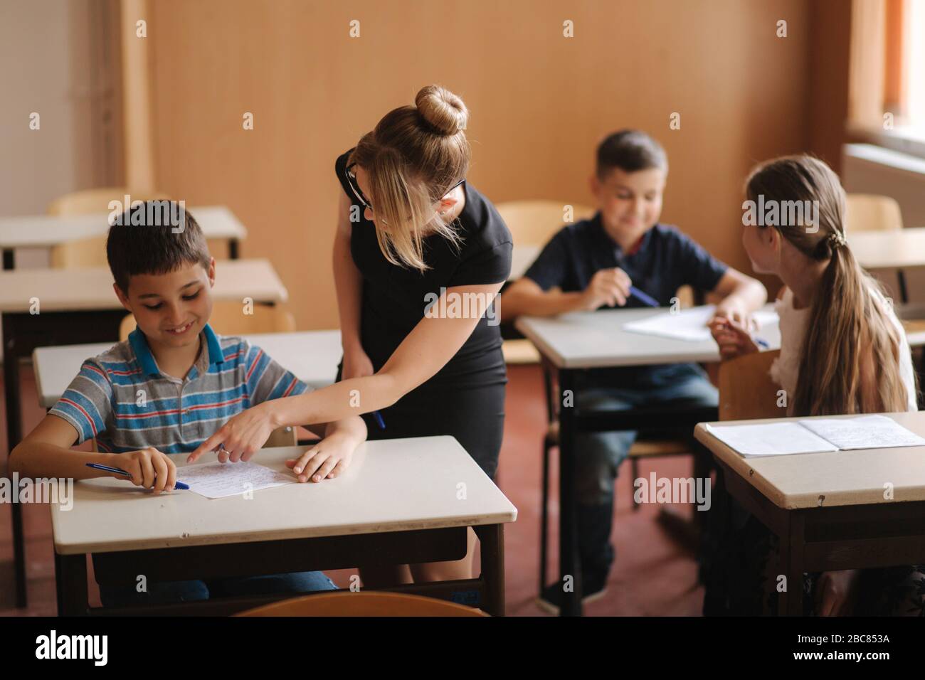 Teacher helping school kids writing test in classroom. education ...