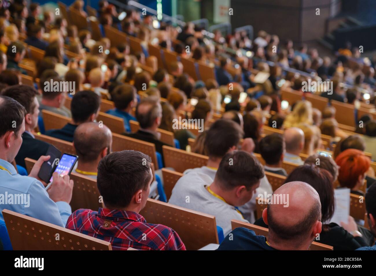 Business conference attendees sit and listen to lecturer, rear top view ...