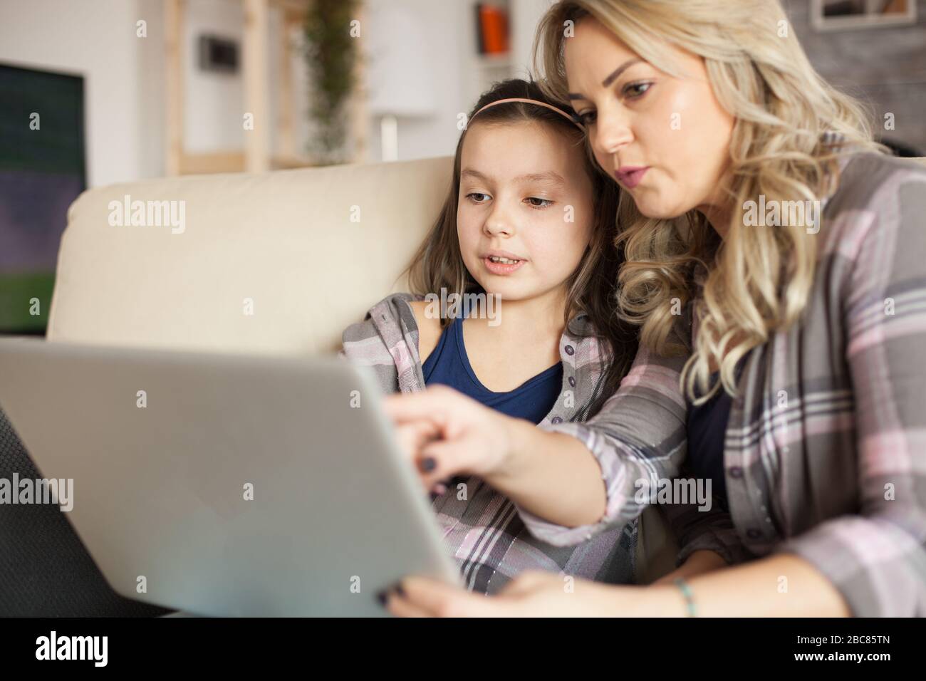 Young mother pointing at laptop while surfing on the internet with her ...