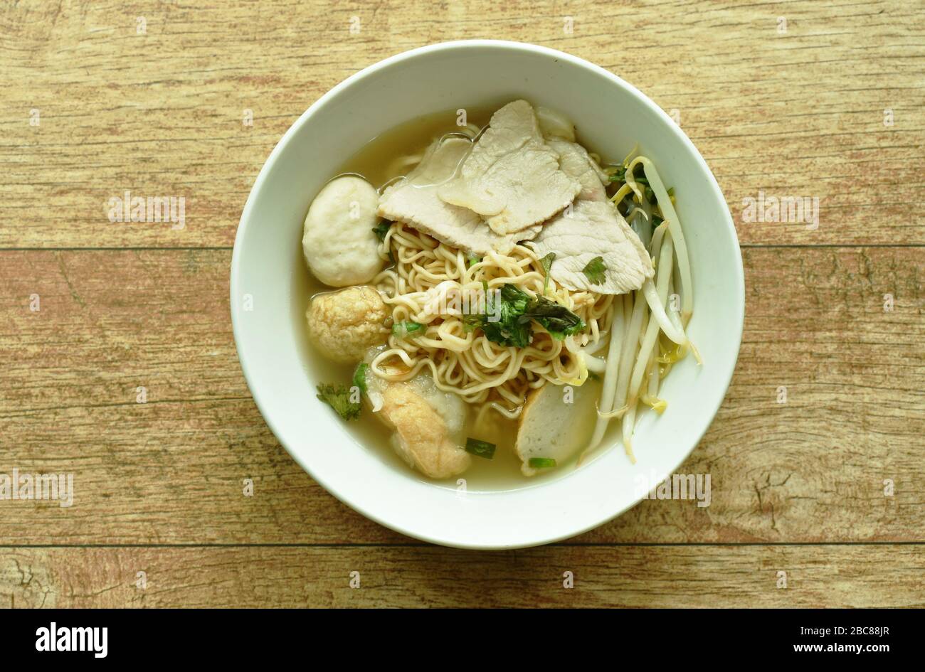 boiled yellow instant noodles topping slice pork and ball in clear soup ...