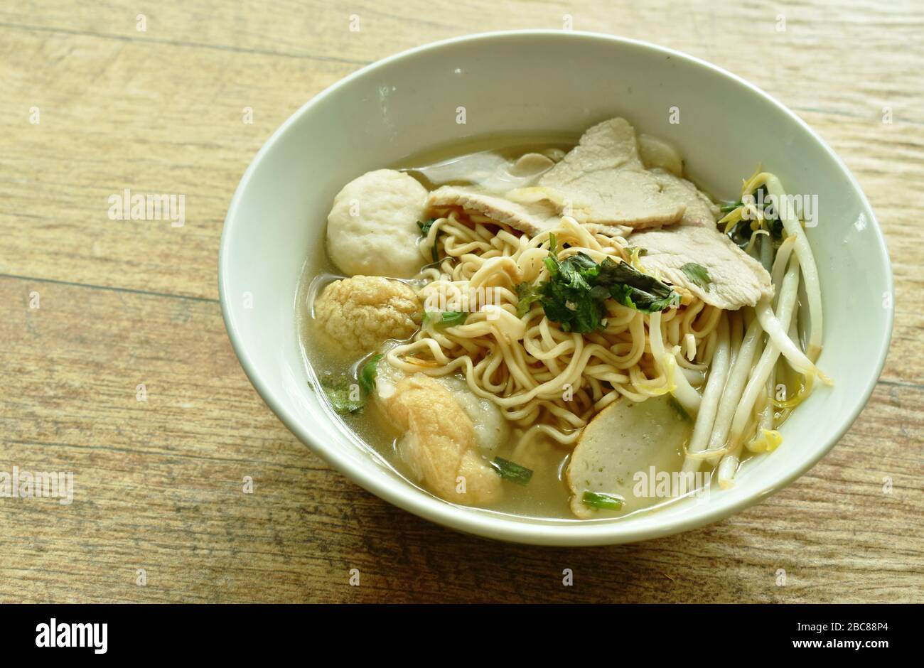 boiled yellow instant noodles topping slice pork and ball in clear soup ...