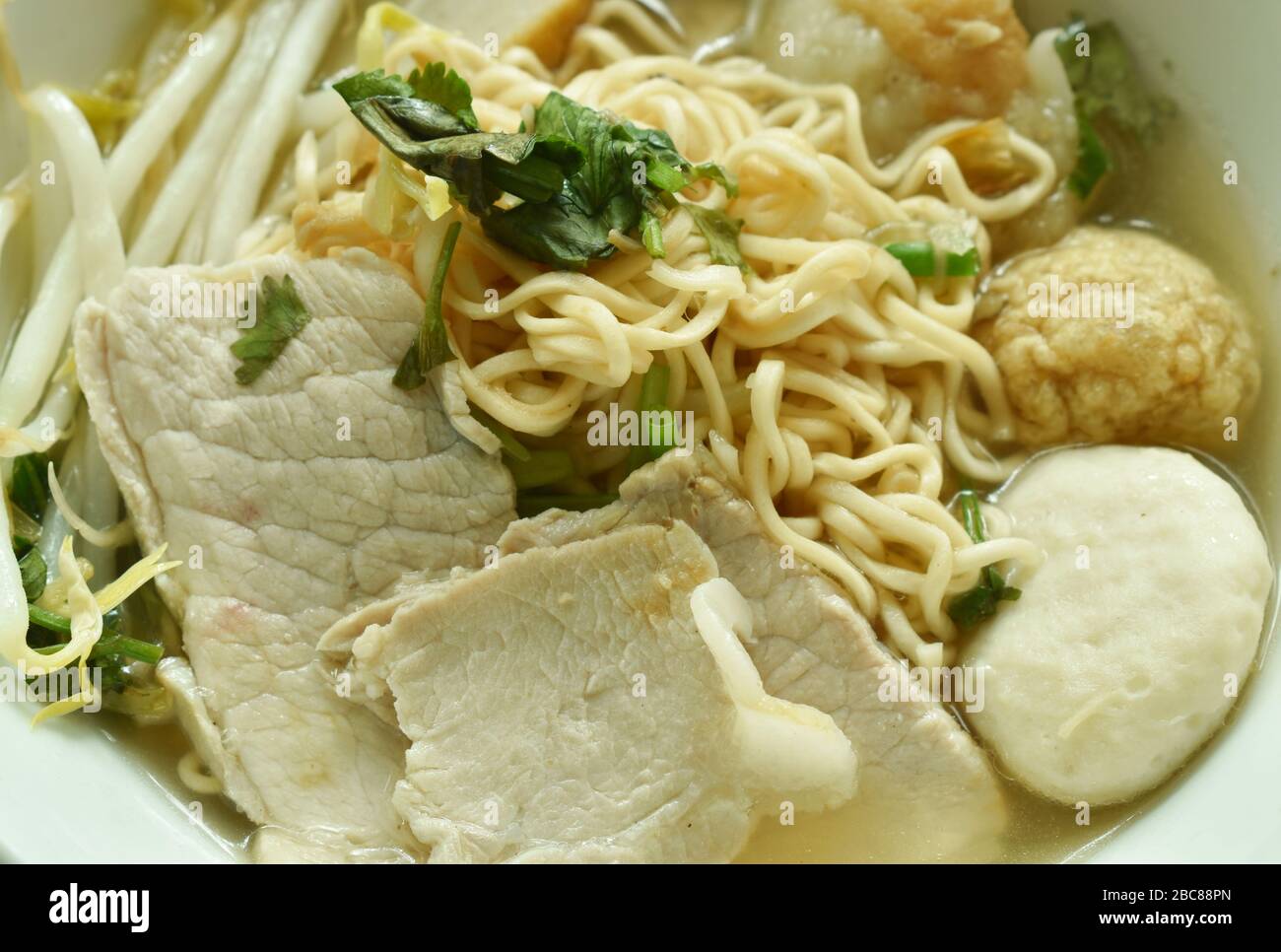 boiled yellow instant noodles topping slice pork and ball in clear soup ...