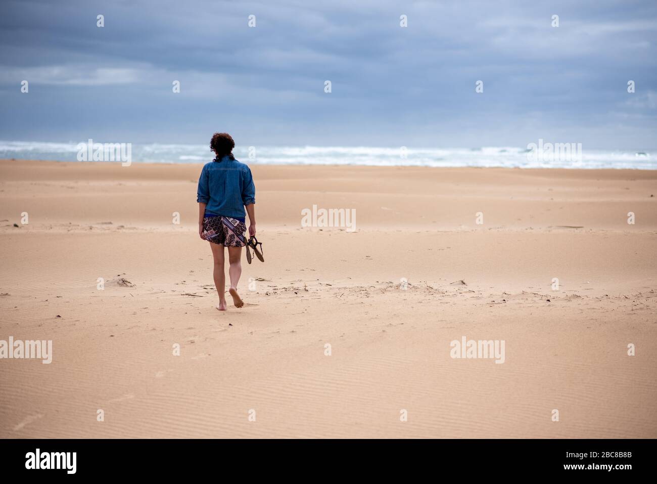 Single woman walking alone on beach Stock Photo - Alamy