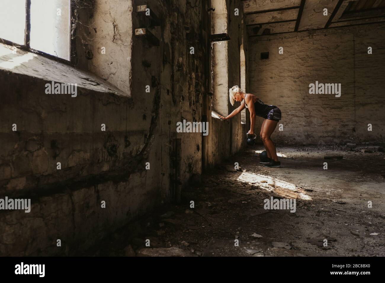 Female athlete workout back by doing kettlebell rows by the window ...