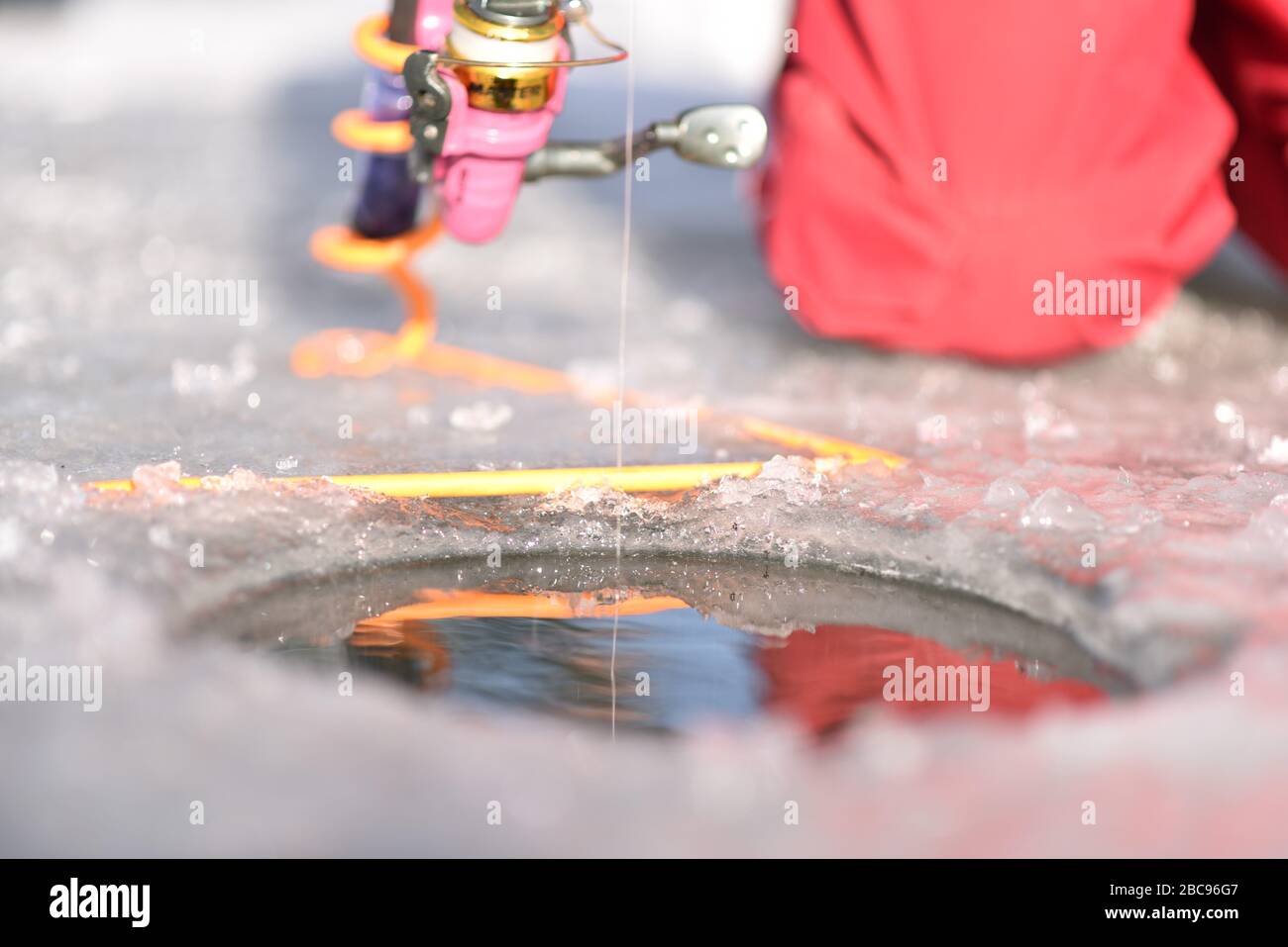 Ice fishing on lake in winter with reflection of fishing pole and ...