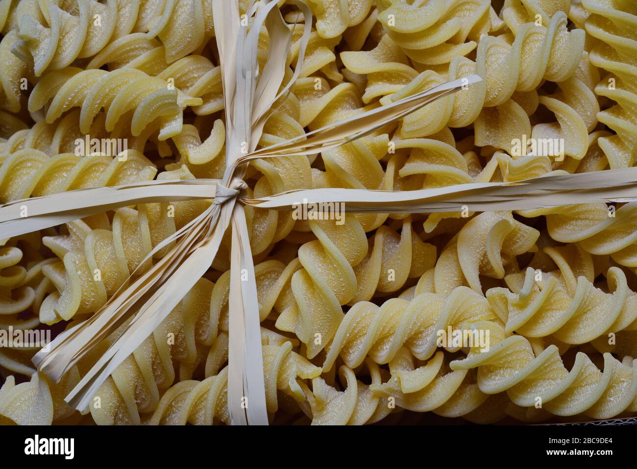 Close-up, background and texture of raw spiral pasta wrapped in a bast ...
