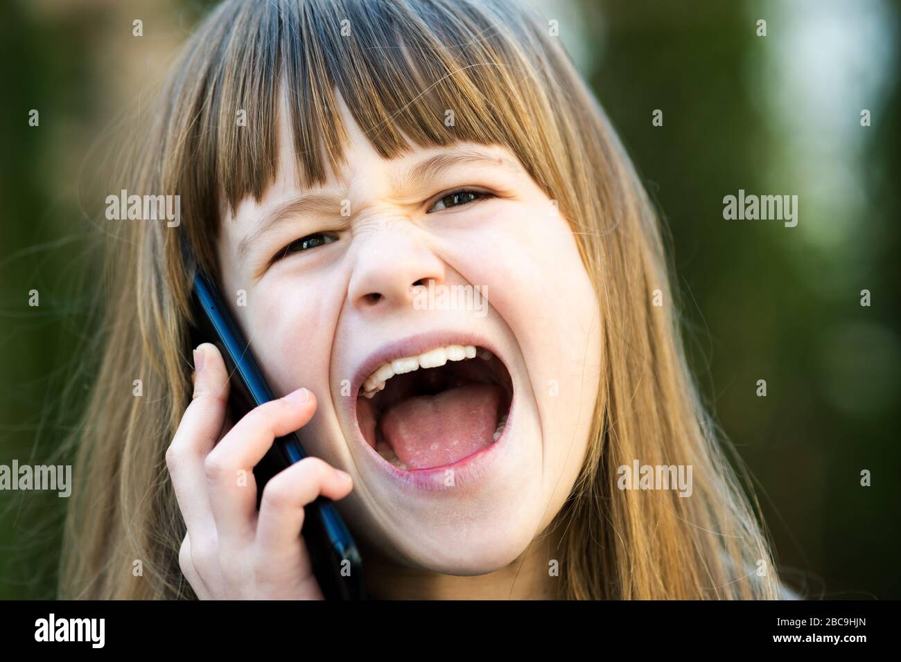 Portrait of angry child girl with long hair talking on cell phone ...
