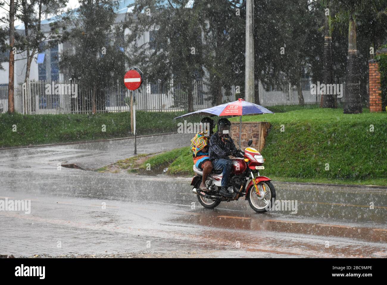 A roofed taxi motorcycle carries a woman in rain on a macadamized road ...