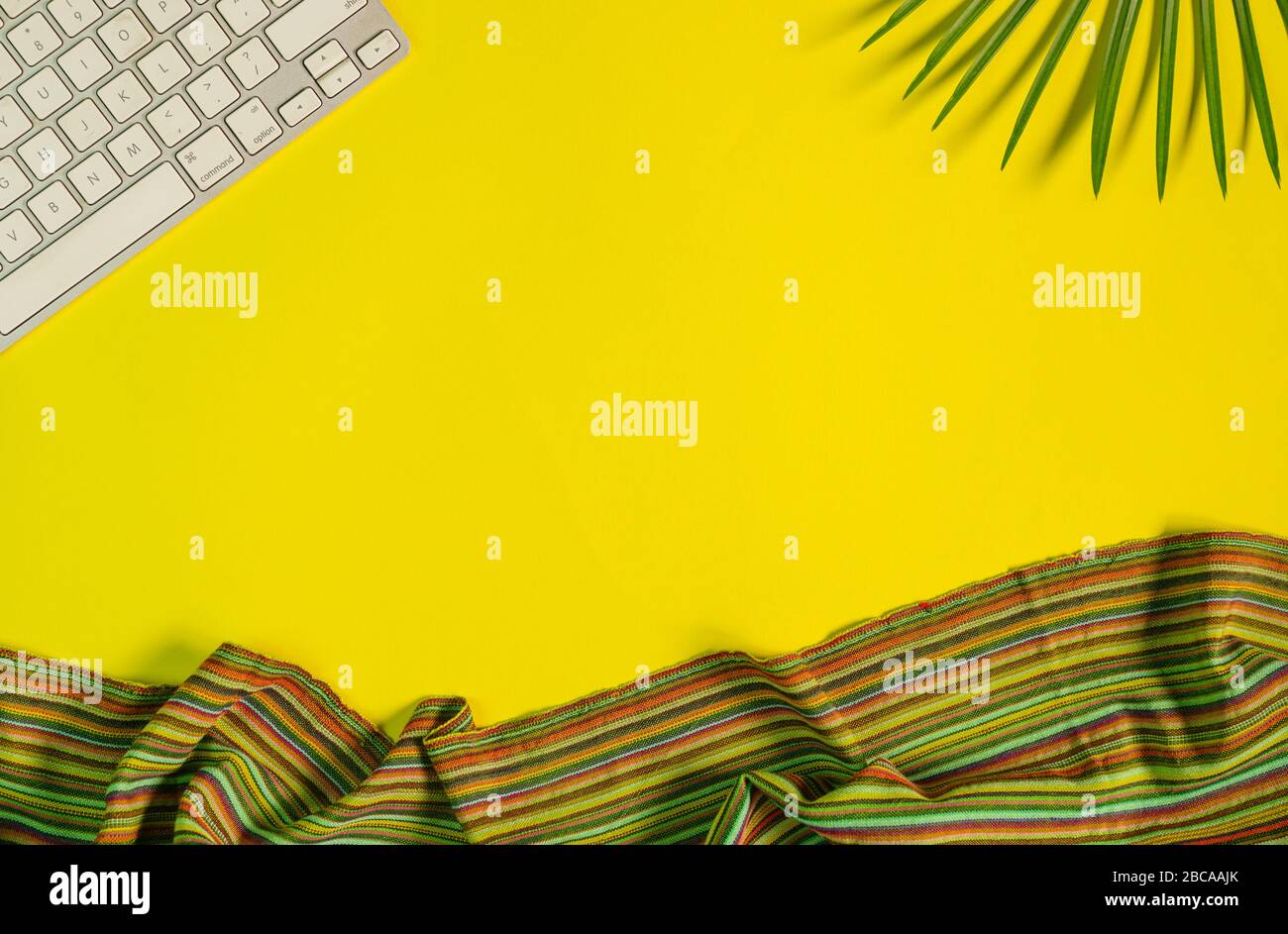 Top view of yellow color office table with keyboard, palm leaves and ...