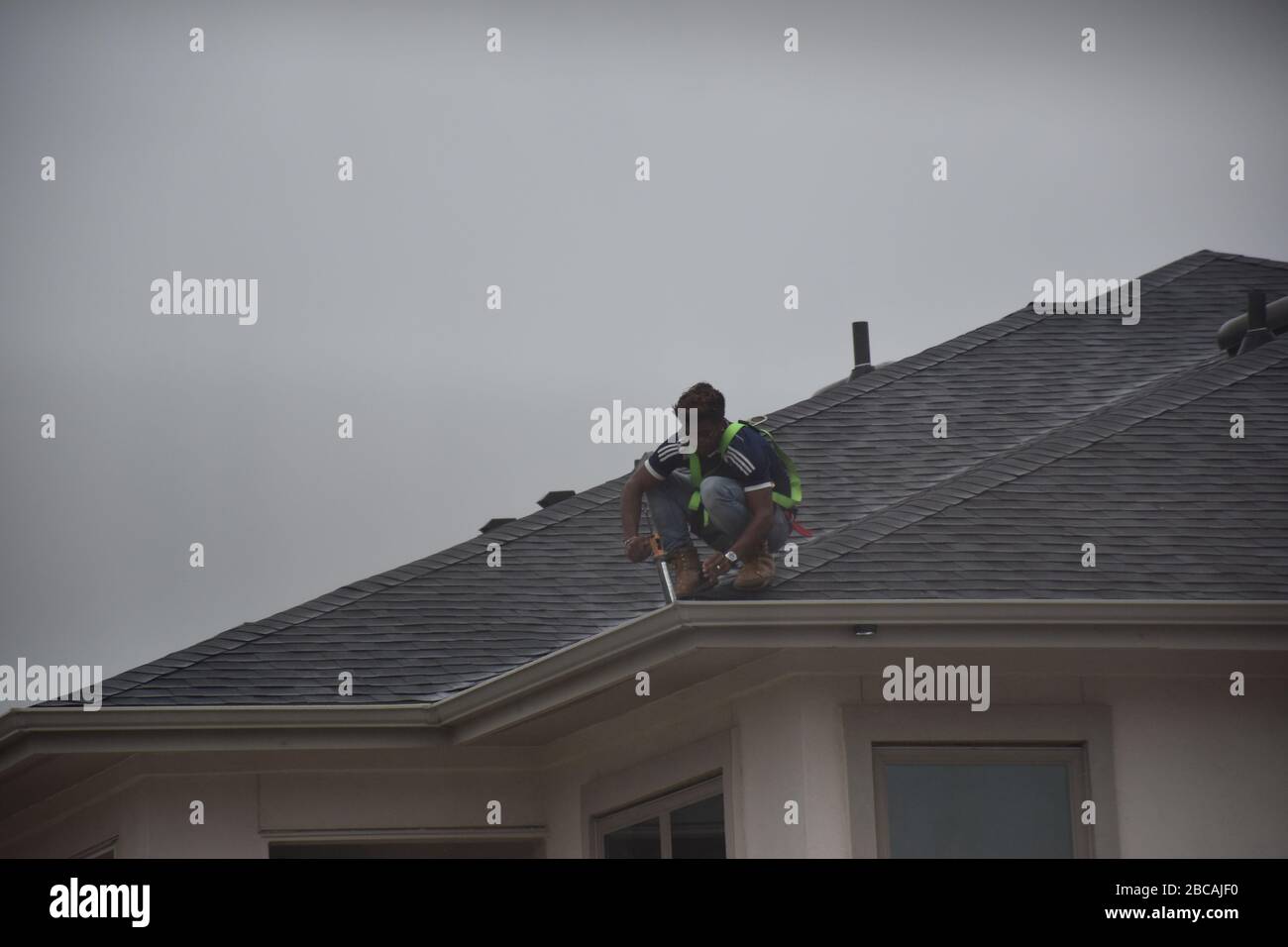 A man contractor worker on roof top working on a cloudy rainy day ...