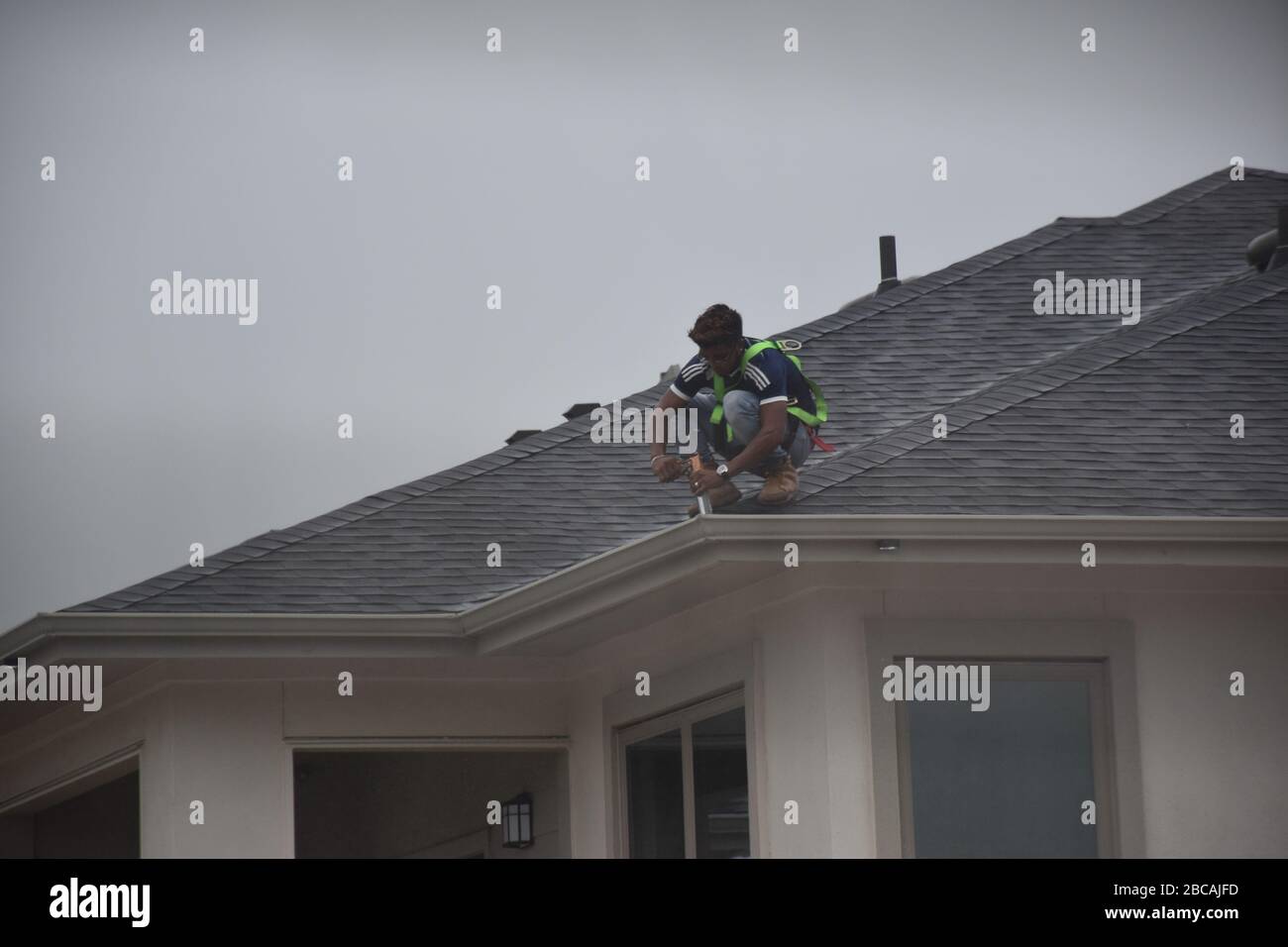 A man contractor worker on roof top working on a cloudy rainy day ...