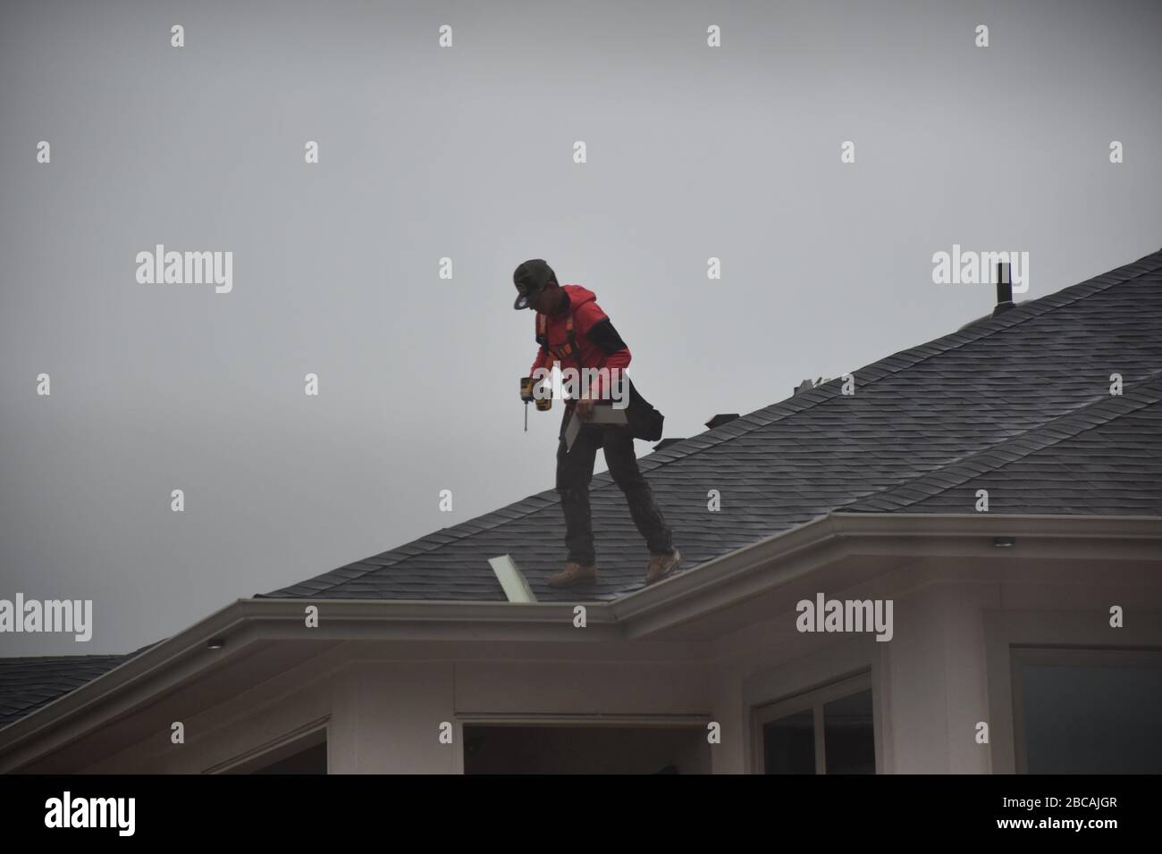 A man contractor worker on roof top working on a cloudy rainy day ...