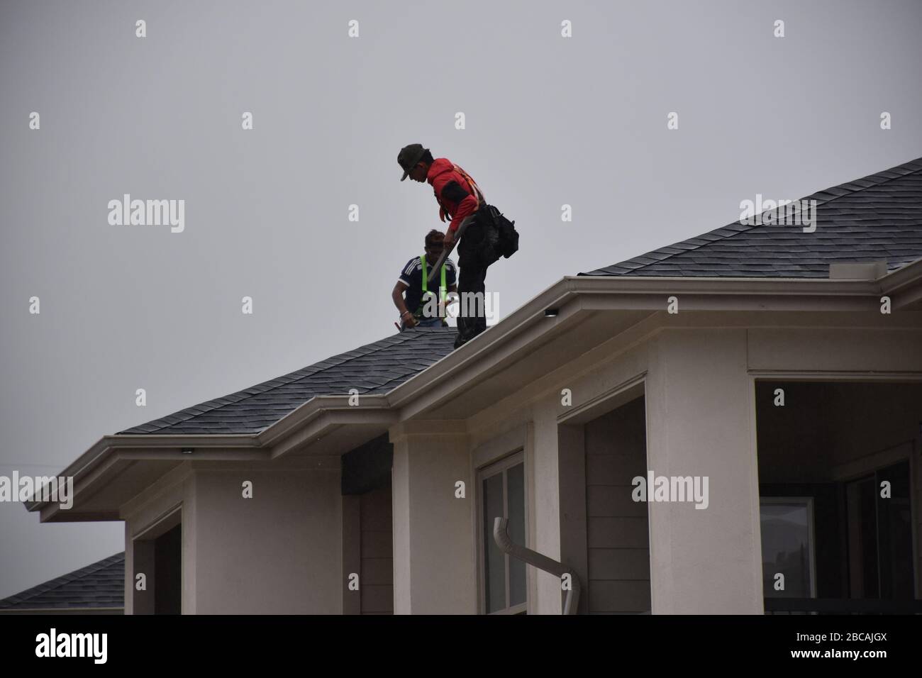 A man contractor worker on roof top working on a cloudy rainy day ...