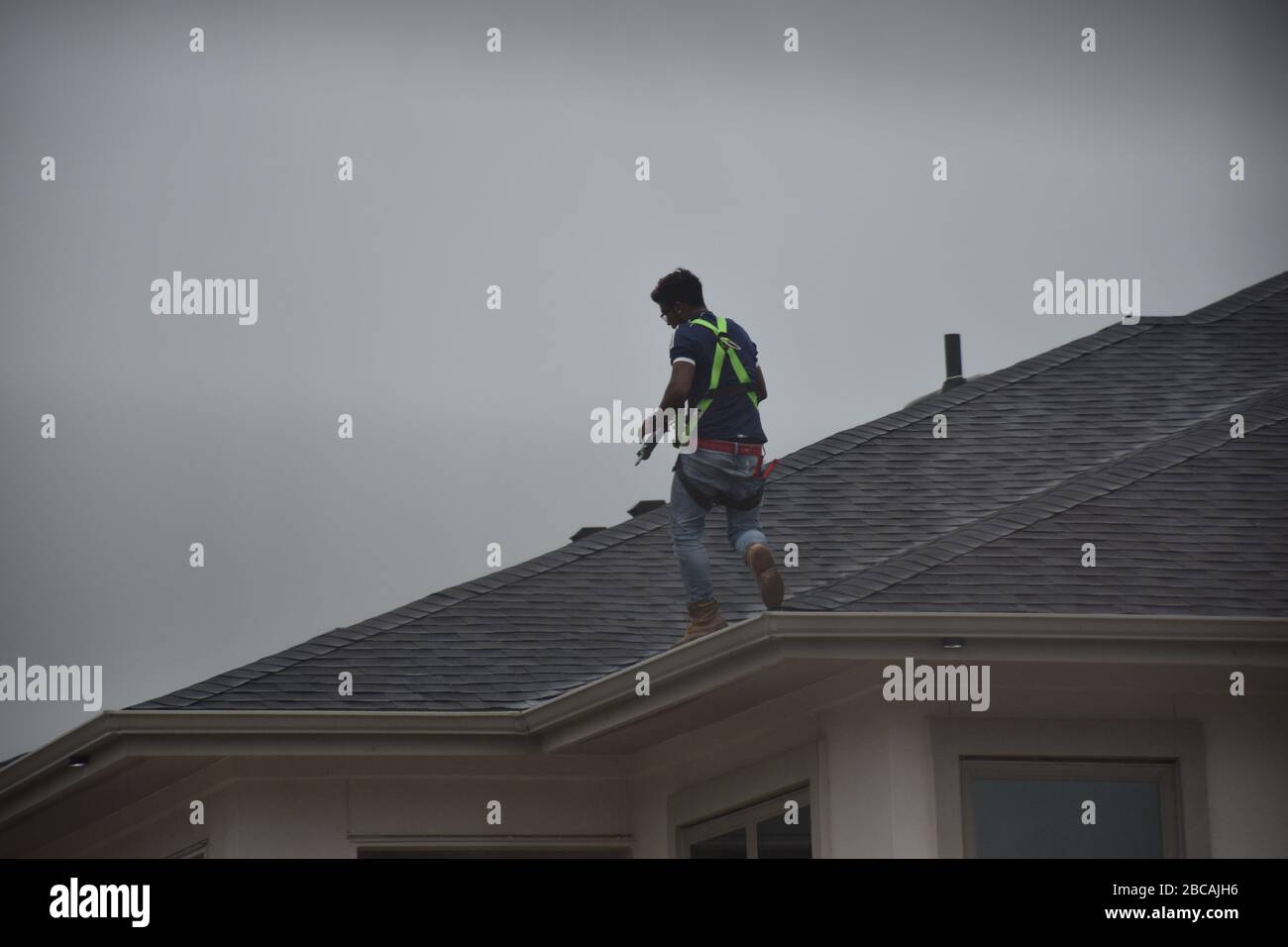 A man contractor worker on roof top working on a cloudy rainy day ...