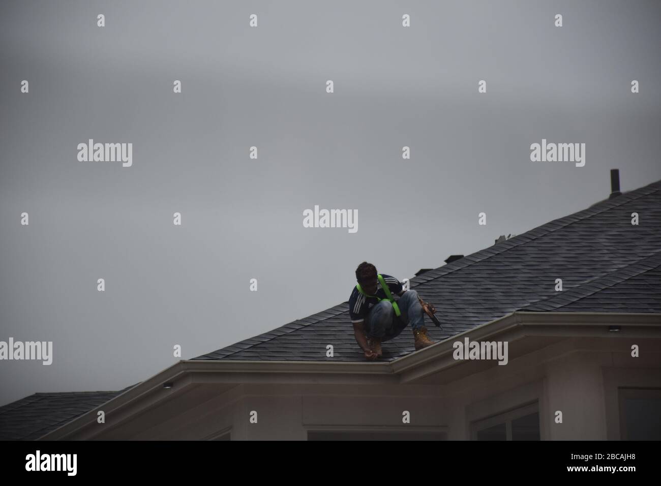 A man contractor worker on roof top working on a cloudy rainy day ...